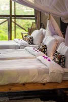 Uma cama com dossel, vários travesseiros e vista para o verde lá fora.
