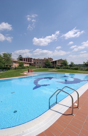 Piscina com padrão de azulejos, rodeada por um deck de tijolos e um edifício ao fundo.