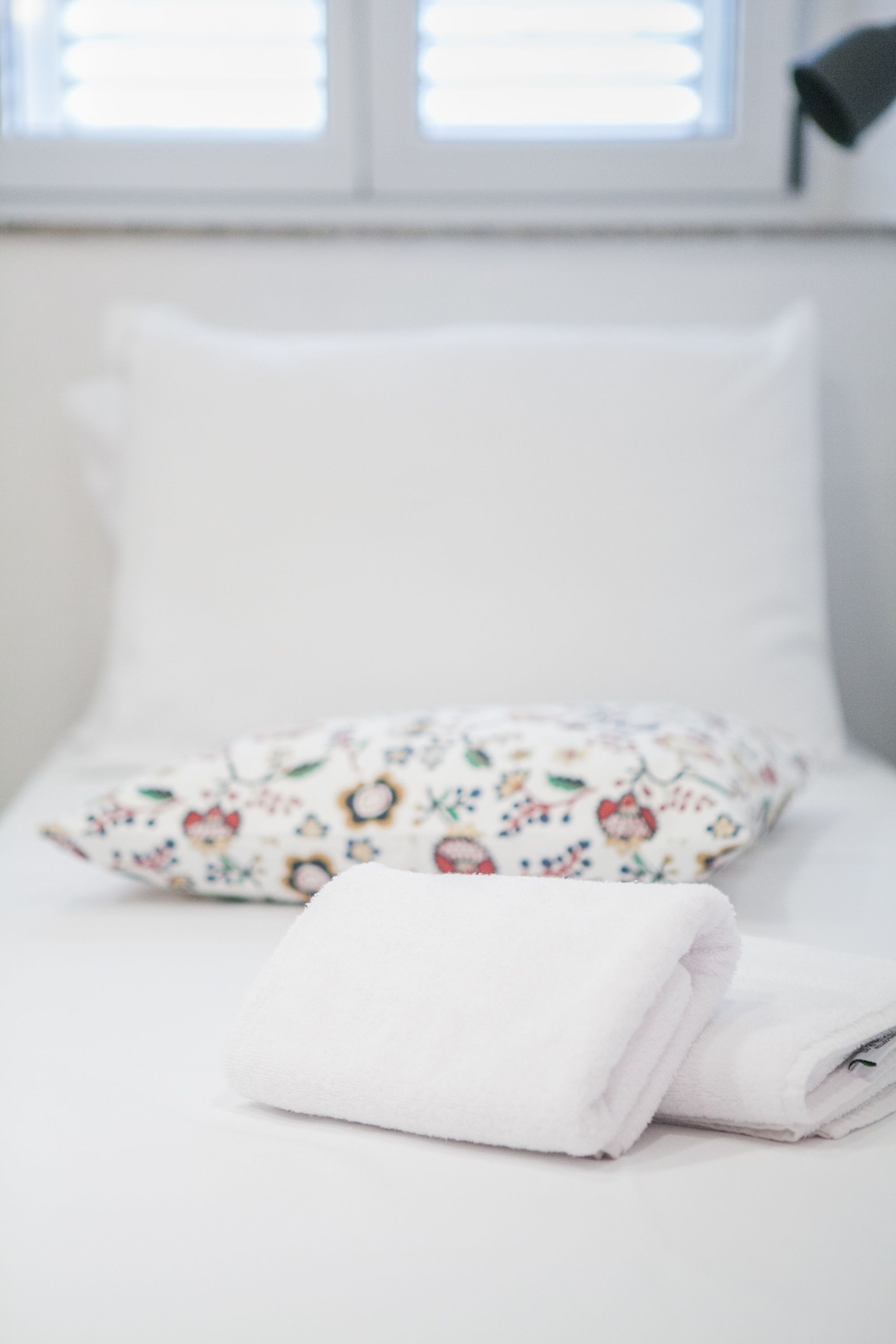 Uma cama bem arrumada com roupa de cama branca e um travesseiro estampado com motivos florais.