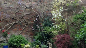 Um jardim com diversas plantas e flores, uma parede de tijolos e uma estátua.