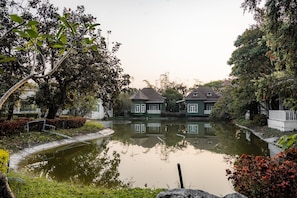 Um corpo d'água calma refletindo casas, cercado por vegetação e um caminho.