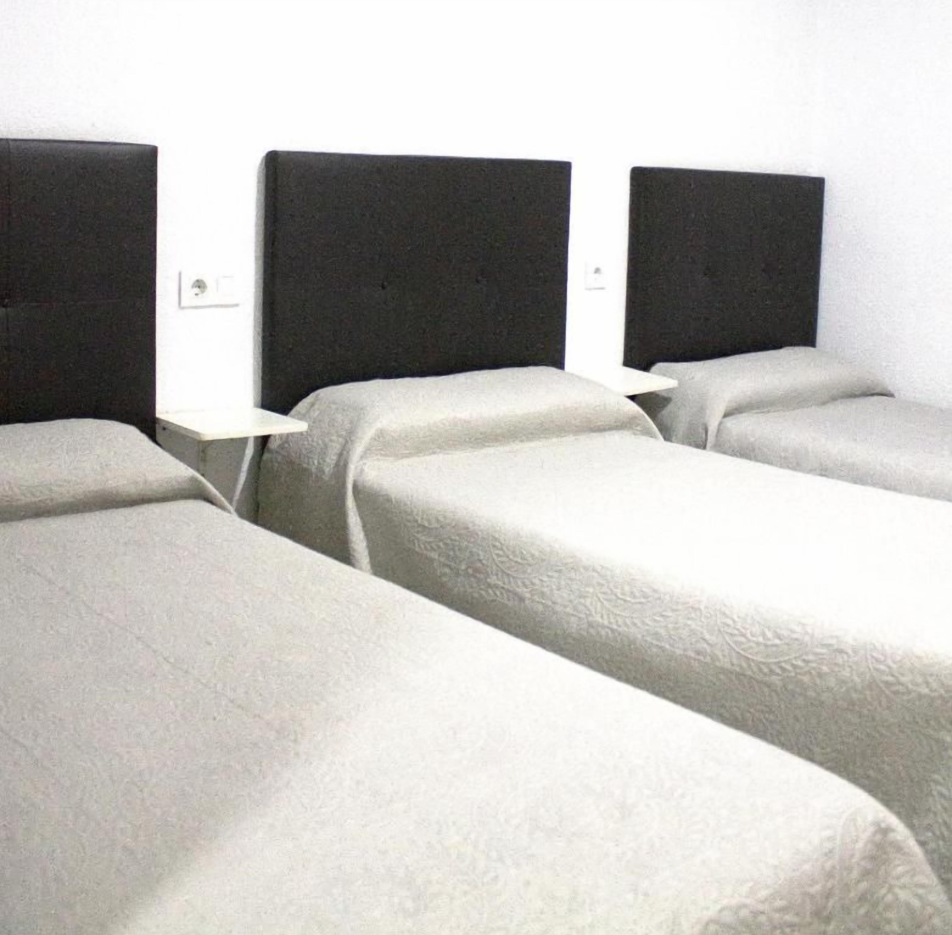 Quarto com três camas enfileiradas, cada uma com cabeceira e mesa de cabeceira.