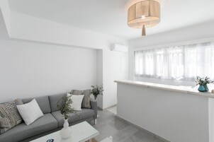 Uma sala de estar moderna com um sofá cinzento, uma mesa de centro de vidro e um candelabro de madeira no teto.
