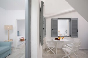 Quarto moderno e bem iluminado, com área de jantar, mesa, cadeiras, sofá e uma luminária.