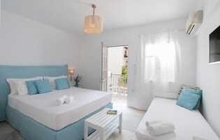 Quarto com uma cama grande, uma cama menor e um banco. Há uma porta que dá para uma área externa.
