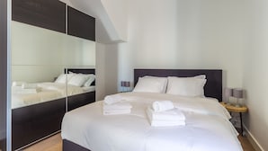 Quarto de hotel moderno com uma cama grande, mesa de cabeceira com luminárias e um espelho grande em uma das paredes.
