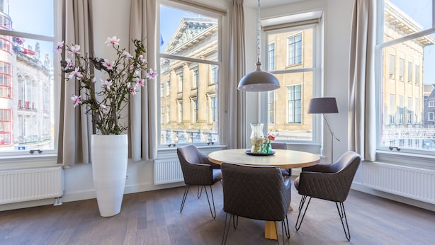 Uma sala de jantar moderna com uma mesa redonda, quatro cadeiras, um vaso grande com flores e um candeeiro suspenso.
