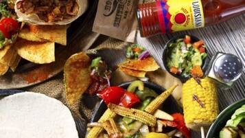 Diversos pratos, incluindo tacos, espiga de milho e uma salada, indicando um ambiente de refeição.