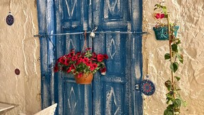 Uma porta azul rústica com um vaso de flores pendurado, uma pequena mesa e um vaso com planta.