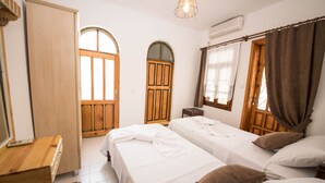 Quarto de hotel com duas camas, portas de madeira, uma mesa pequena e uma janela com cortinas.