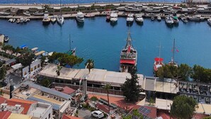 Uma vila costeira com um porto de recreio, edifícios com telhados vermelhos e um céu azul límpido.
