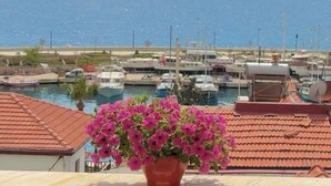 Marina com barcos atracados, vista clara do mar e um edifício com telhado em cerâmica.