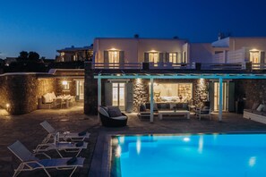 Uma villa moderna com piscina, paredes de pedra e área de estar ao ar livre.