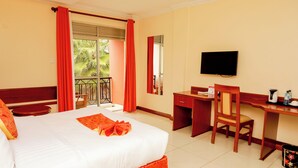 Quarto de hotel com cama, escrivaninha, cadeira, televisão e varanda com cortinas vermelhas.