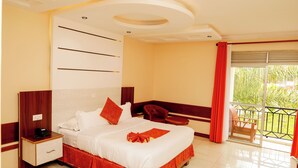 Quarto de hotel com uma cama, mesa de cabeceira, cadeira, varanda com vista para áreas verdes e luminárias circulares no teto.