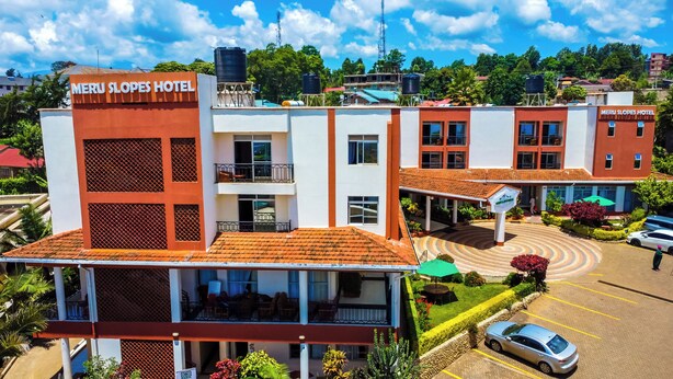 Hotel com design moderno, destacando uma placa visível, várias varandas e uma área de estacionamento.