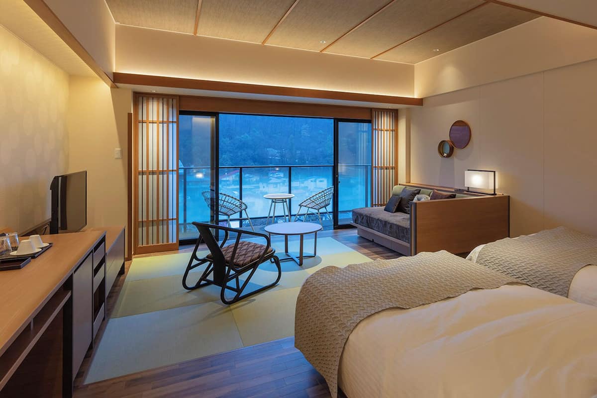 Quarto de hotel com varanda, cama, escrivaninha e televisão.