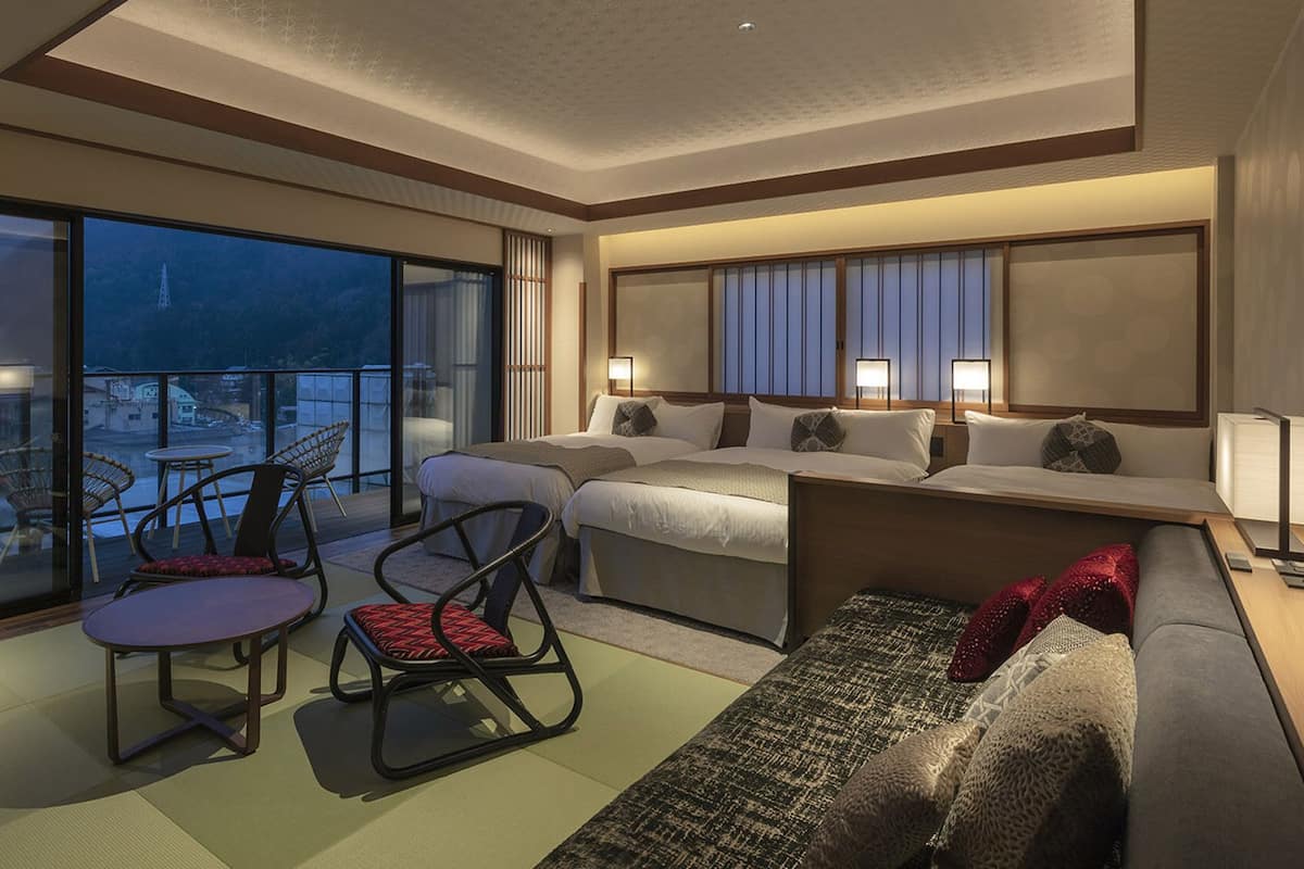 Quarto de hotel com varanda, cama, sofá e mesa de jantar.
