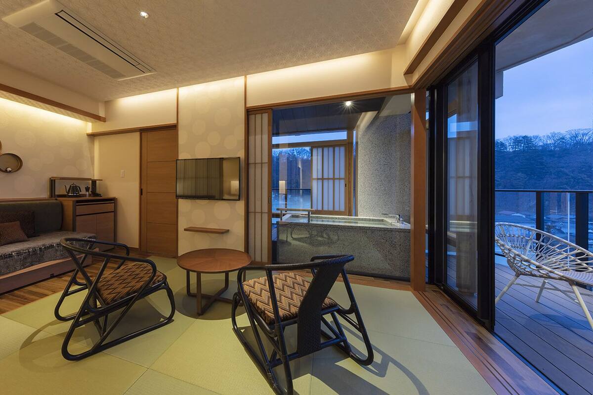 Um interior moderno com sofá, duas cadeiras, uma mesinha, televisão e uma varanda com vista.