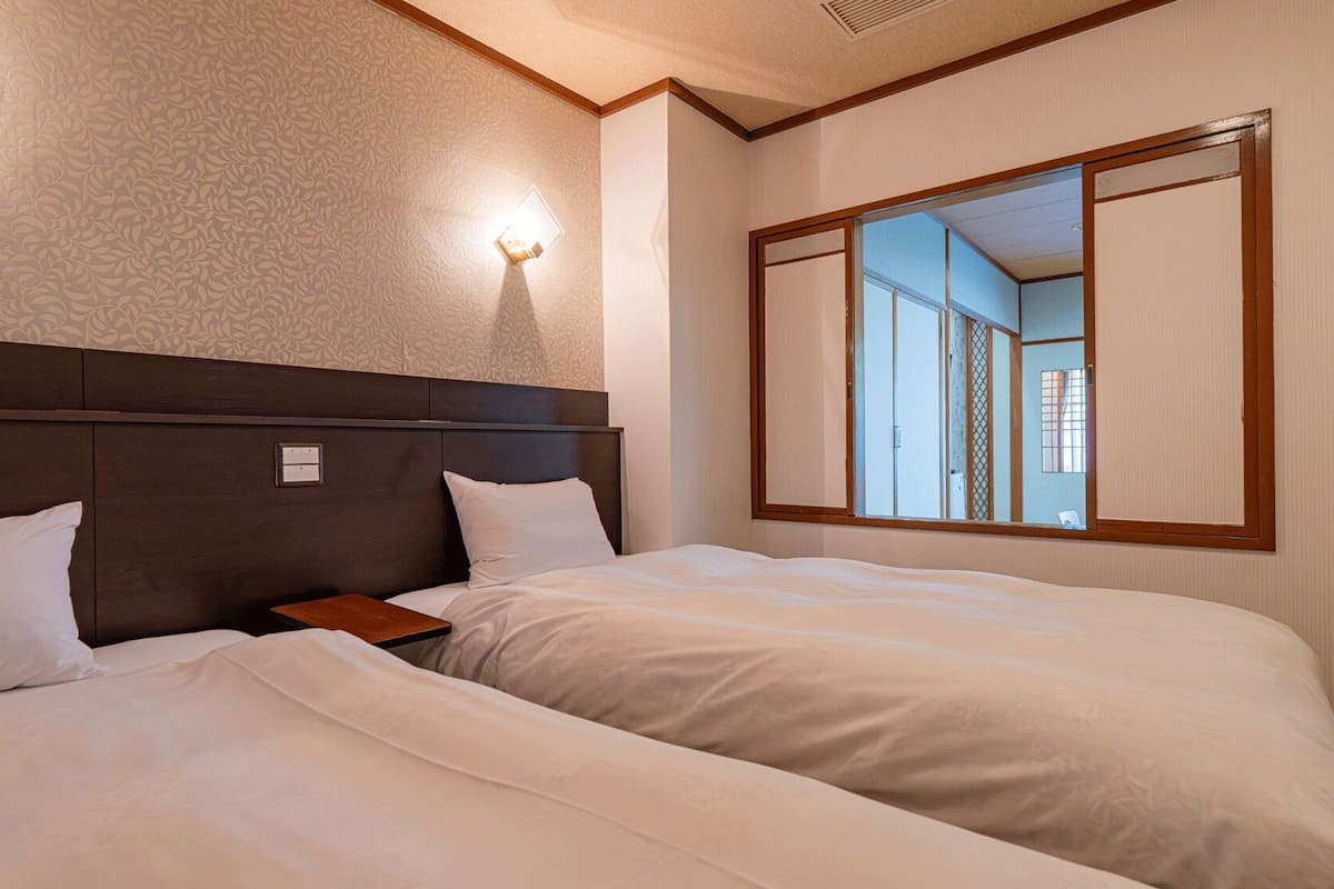Quarto de hotel com uma cama grande, uma mesinha de cabeceira, uma luminária na parede e um espelho grande que reflete o quarto.