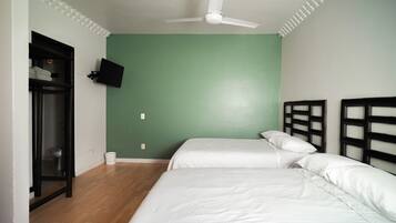 Quarto com duas camas, ventilador de teto, televisão e um pequeno armário.