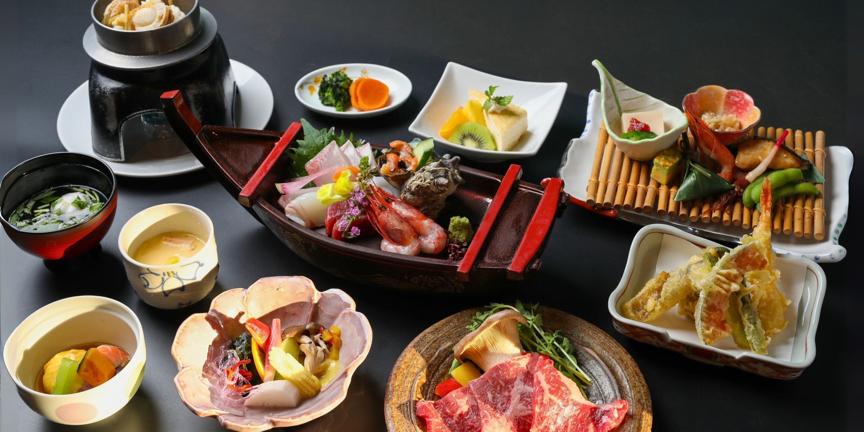 Diversos pratos, incluindo frutos do mar, legumes e carne, dispostos sobre uma mesa com um conjunto de chá japonês tradicional.