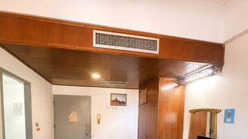 Um quarto com piso de madeira, uma mesa com cadeiras, uma televisão, um pequeno frigorífico e uma porta que dá para outro quarto.