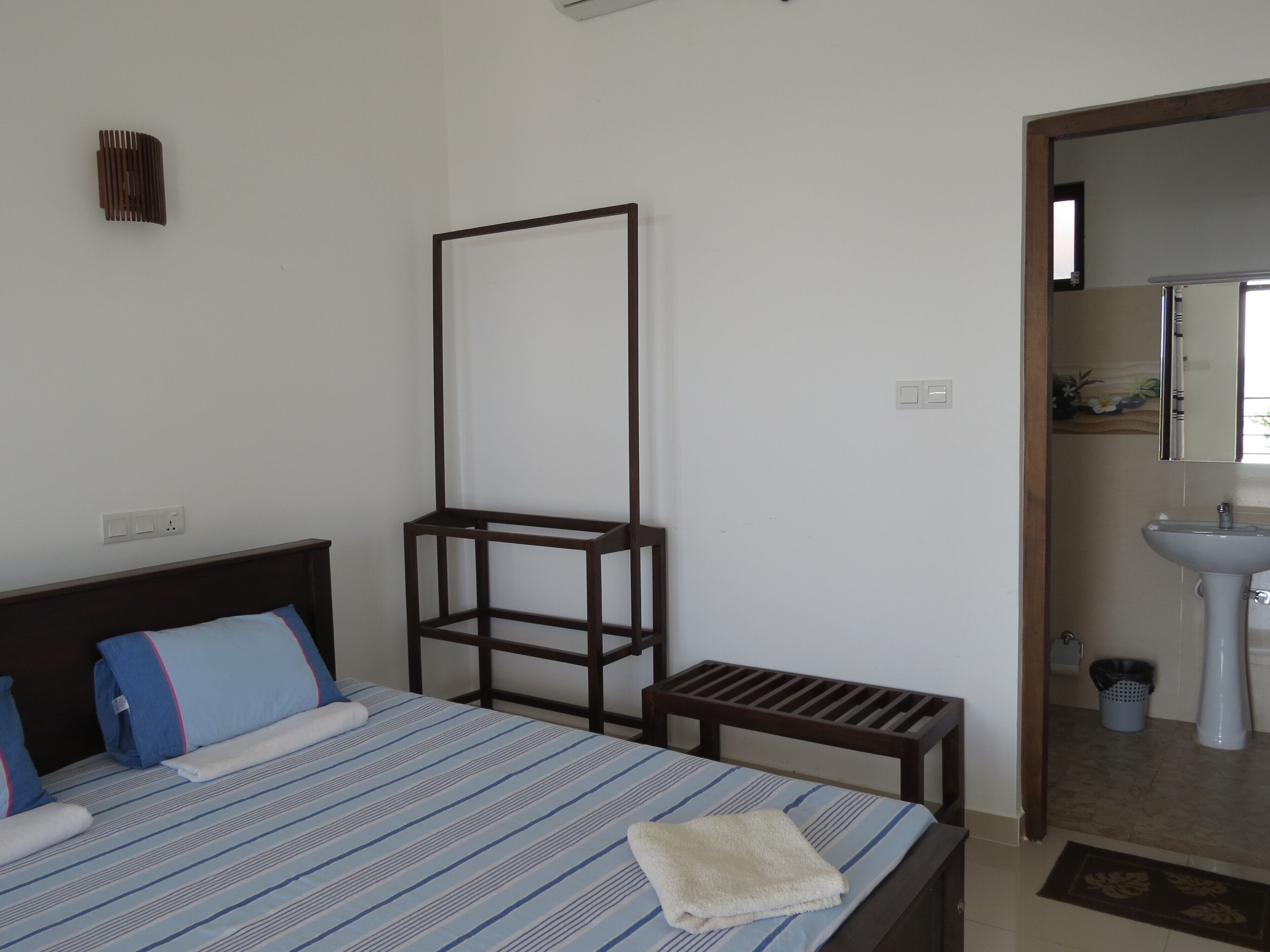 Quarto com cama, mesa de cabeceira, espelho e banheiro visível por uma porta aberta.