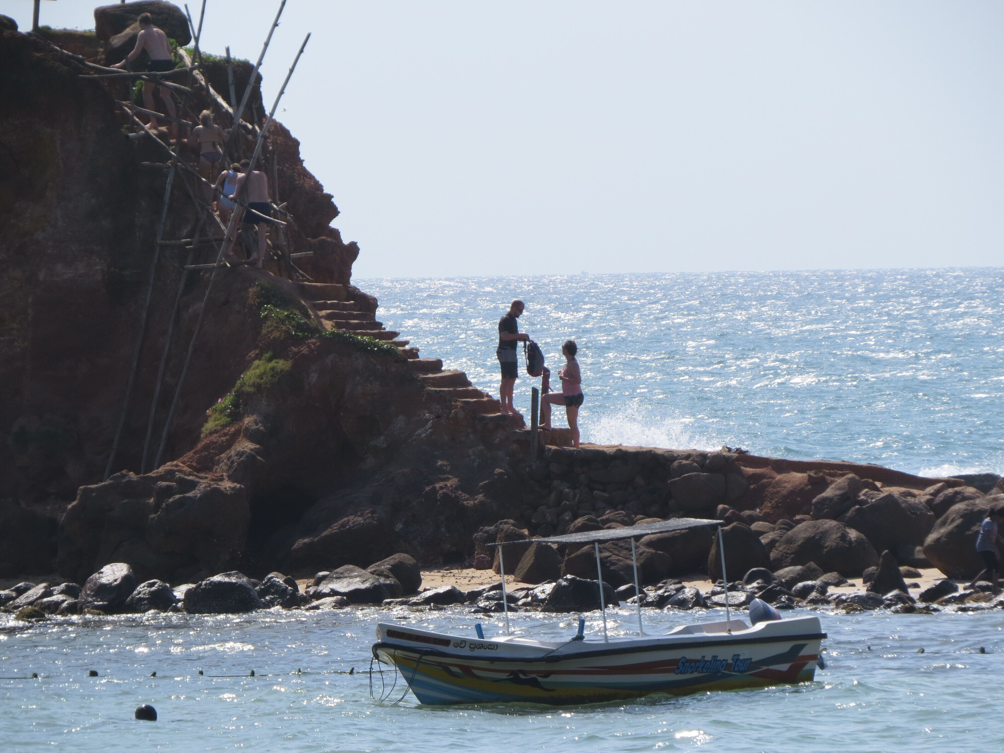 Litoral rochoso com um barco chamado 'Snorkeling Tour' ancorado perto da costa.