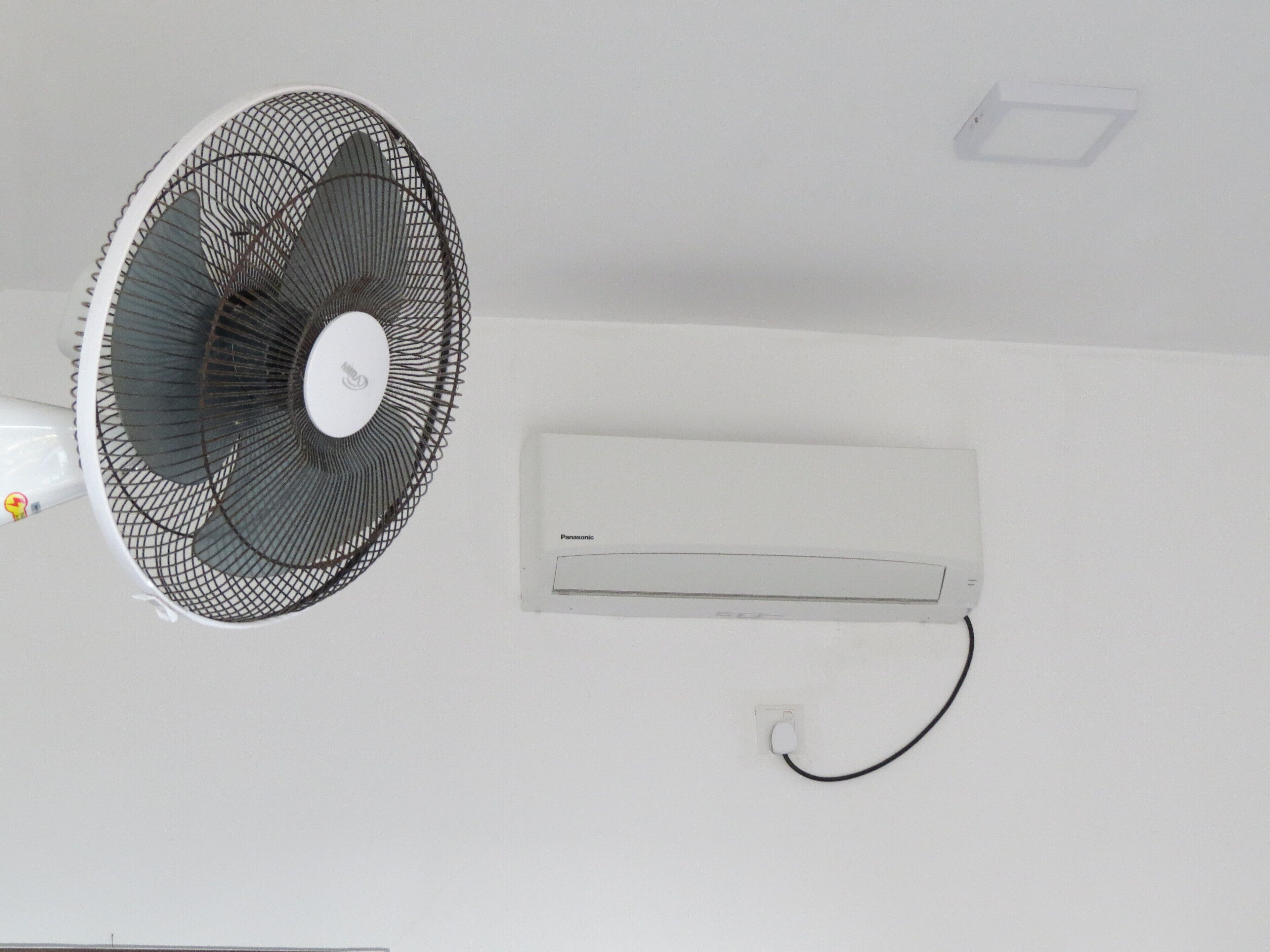 Um ventilador de teto e um aparelho de ar condicionado fixados em uma parede branca.