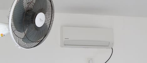 Um ventilador de teto e um aparelho de ar condicionado fixados em uma parede branca.