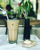 Um copo de café gelado com canudo, um vaso escuro com uma planta e um biscoito sobre um guardanapo.