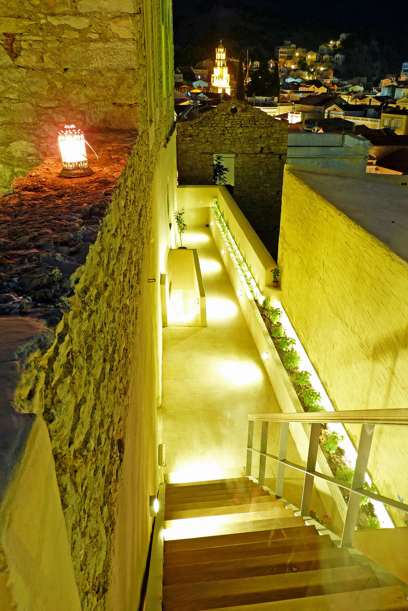 Uma escadaria com uma parede de pedra de um lado e vista para uma cidade à noite.