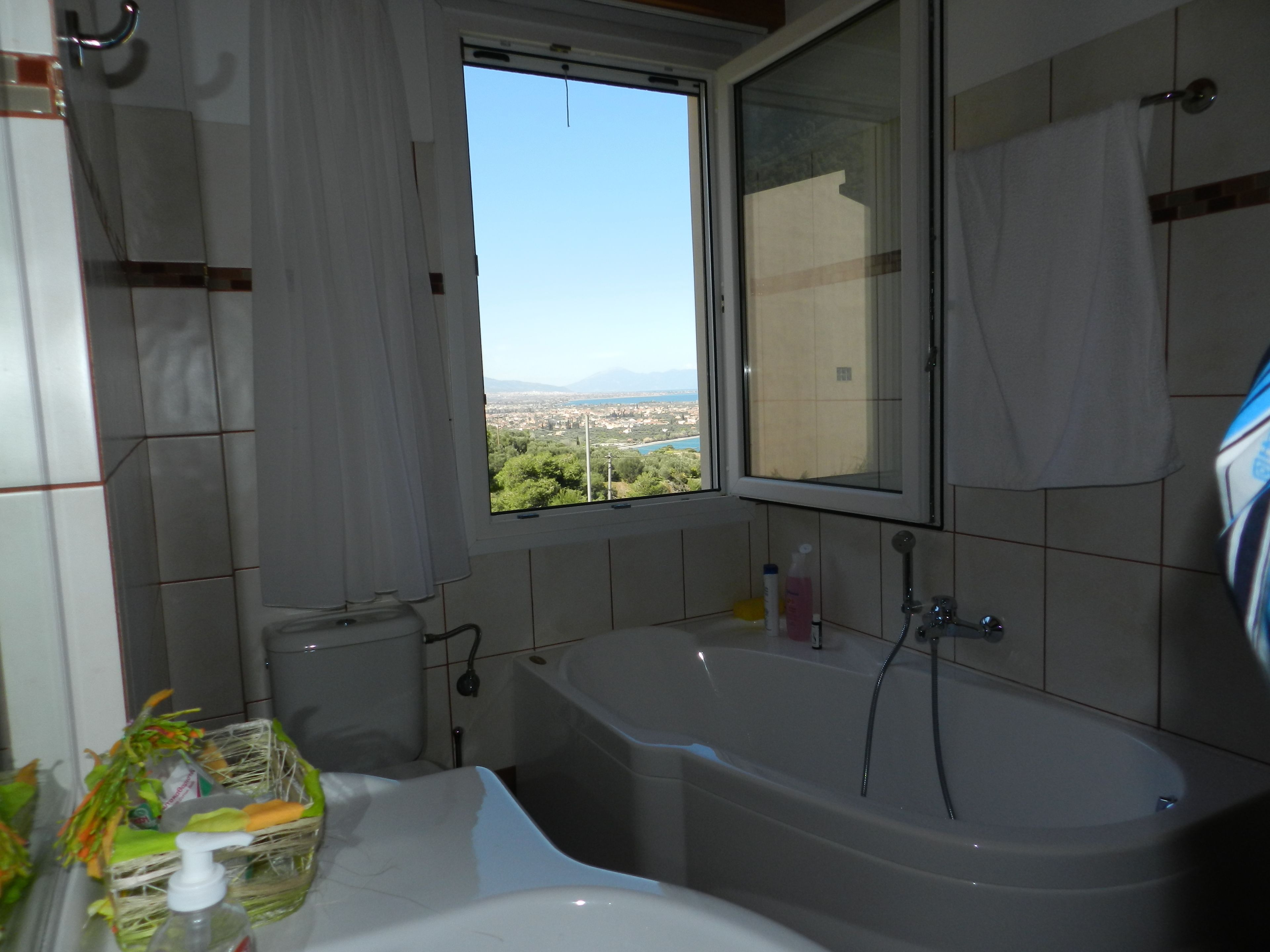 Casa de banho com banheira, janela com vista para a cidade e lavatório com artigos de higiene pessoal.