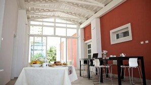 Uma área de refeições com uma mesa posta para dois, uma janela com vista para o verde e uma parede vermelha.