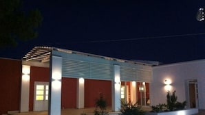 Um edifício moderno com entrada coberta, fachada bem iluminada e calçada pavimentada.
