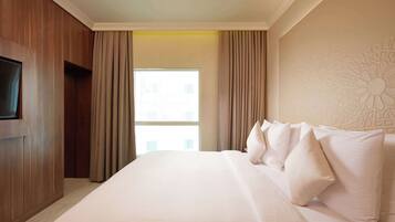 Quarto de hotel com uma cama grande, televisão de tela plana na parede e uma janela com cortinas.