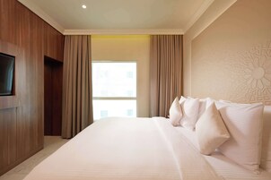 Quarto de hotel com uma cama grande, televisão de tela plana na parede e uma janela com cortinas.