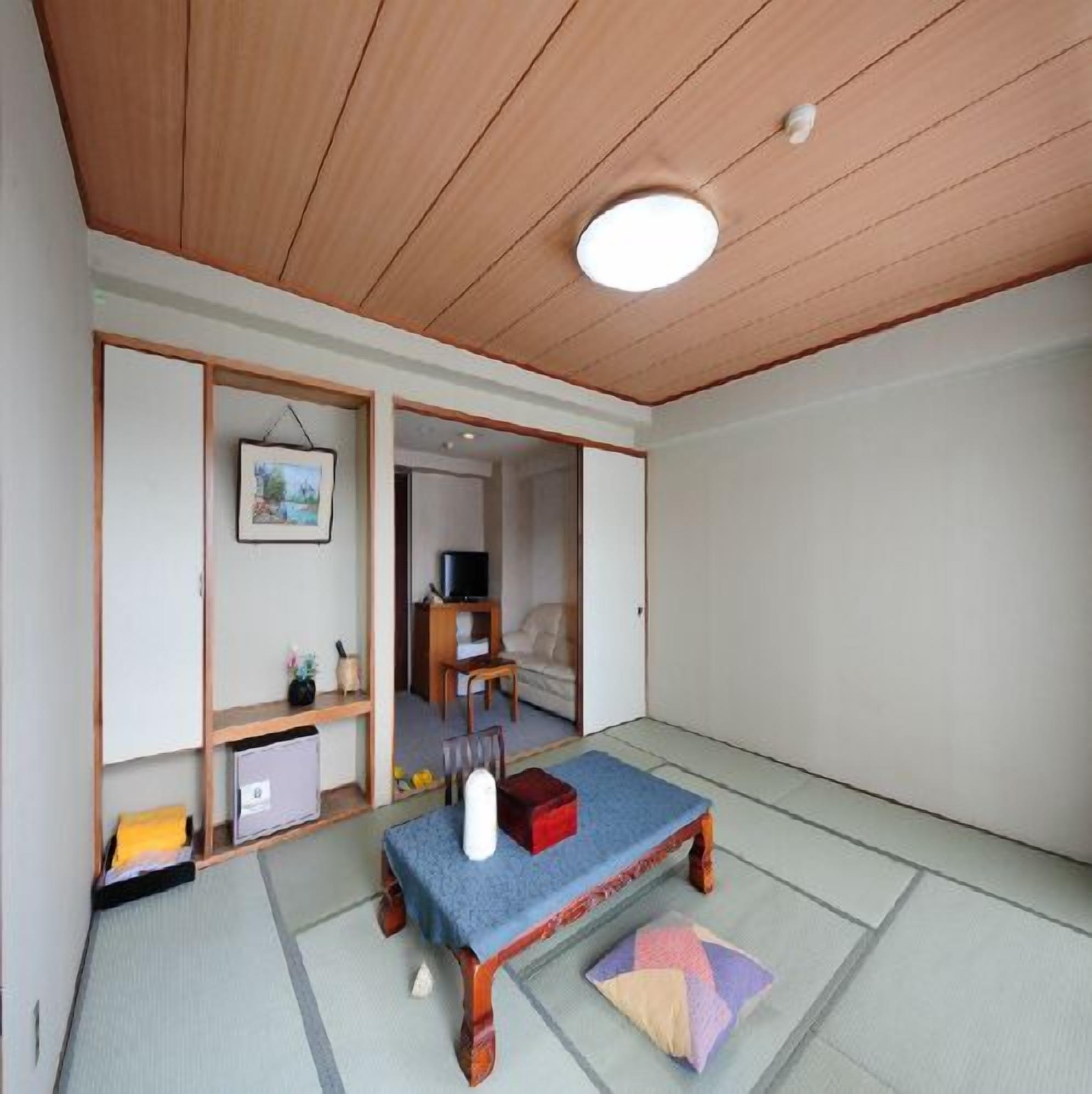 Um quarto em estilo japonês tradicional, com tatames, cama de madeira baixa, televisão e portas deslizantes.