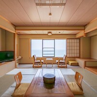 Quarto em estilo japonês tradicional, com tatames, uma mesa baixa com almofadas e uma televisão à esquerda.