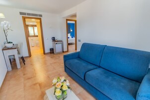 Uma sala de estar com um sofá azul, uma mesinha com um vaso de flores e vista para a cozinha.