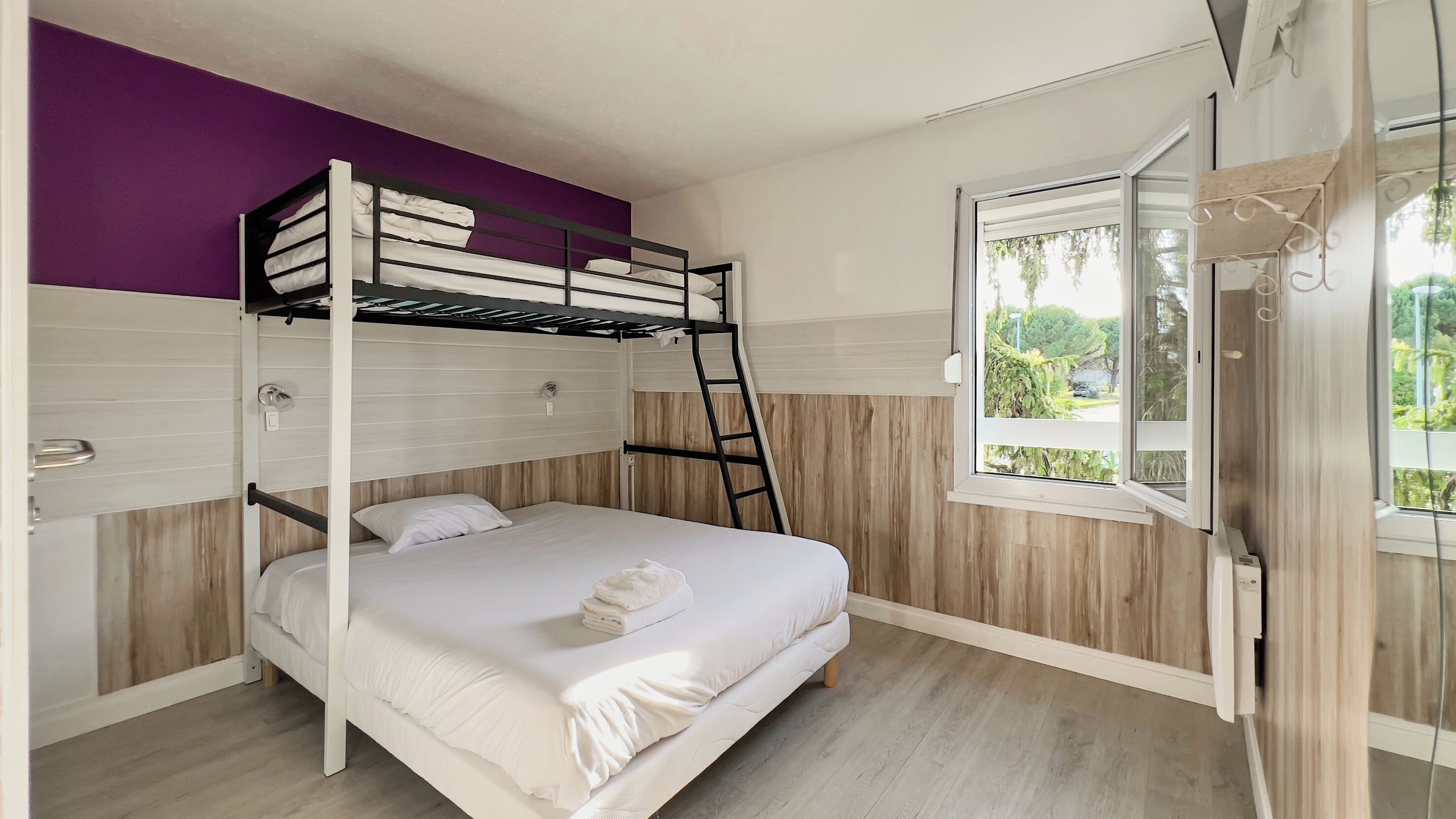 Quarto com beliche, janela, paredes de painel de madeira e porta.