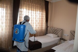 Uma pessoa usando um purificador de ar azul num quarto de hotel com duas camas e uma mesa de cabeceira.