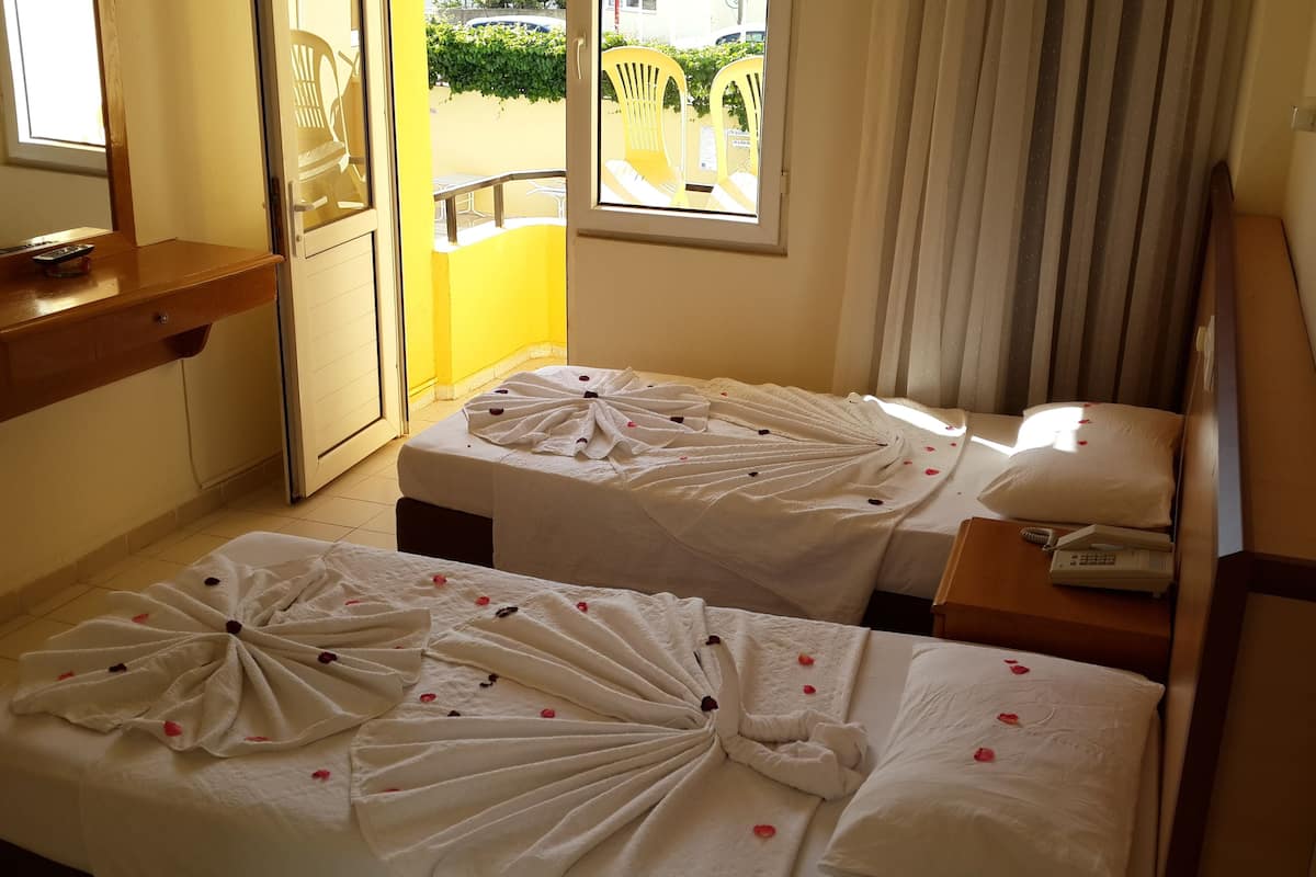 Quarto de hotel com duas camas, cada uma decorada com uma toalha dobrada em formato de leque, e uma mesa de cabeceira com telefone.
