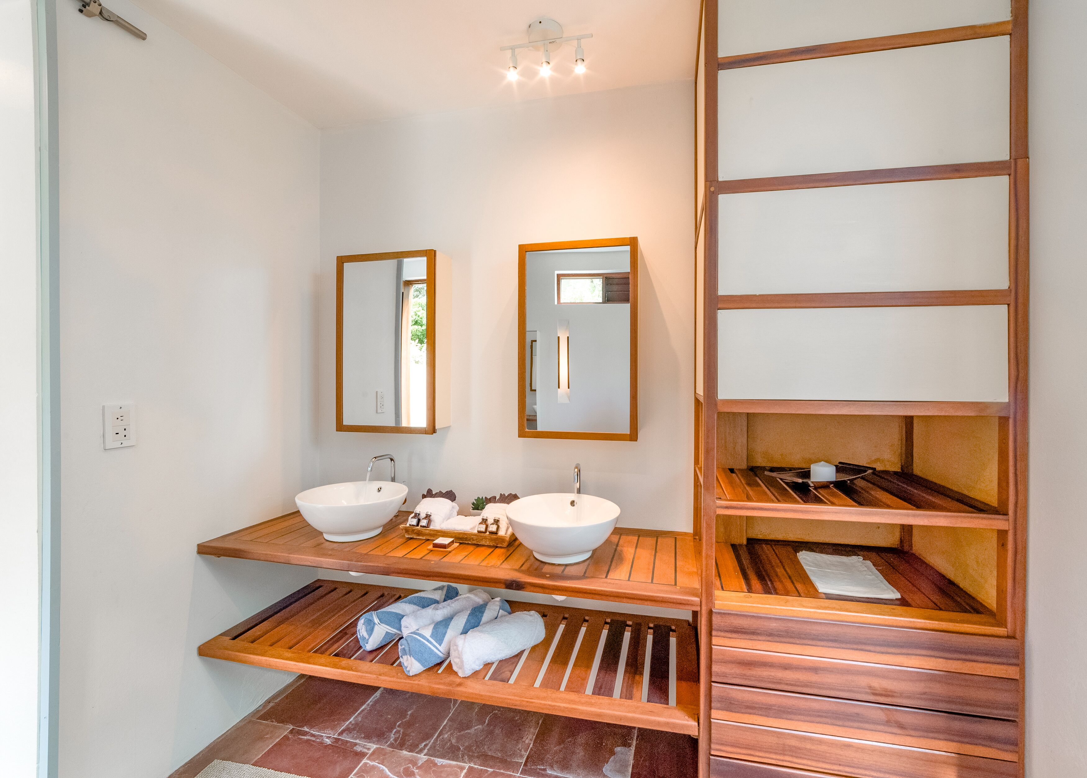 Casa de banho com duas pias, estantes de madeira e um porta-toalhas.