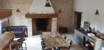 Um quarto rústico com parede de pedra, lareira, mesa de madeira com cadeiras, sofá de couro e área de cozinha com armários e bancada.