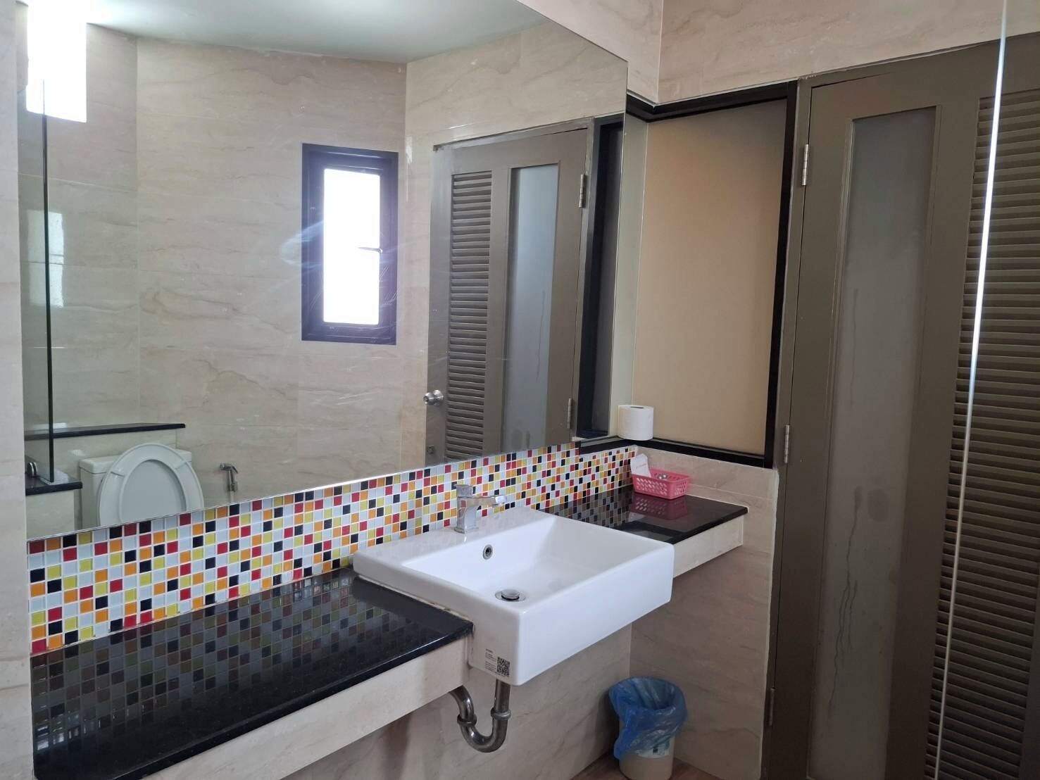 Um banheiro com painel de azulejos, pia branca, espelho e vaso sanitário.