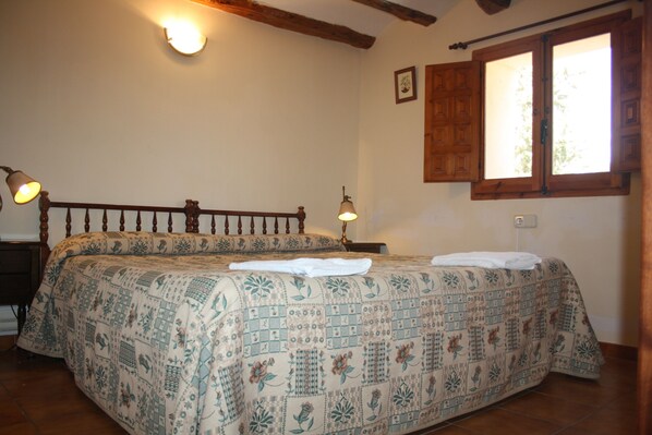 Quarto com cama de madeira, duas luminárias de cabeceira, uma janela com persianas de madeira e um edredom estampado.