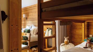 Quarto com beliche de madeira, cabeceira de madeira, uma pequena prateleira com objetos e um urso de pelúcia na cama.