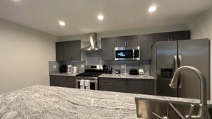 Cozinha moderna com bancadas de granito, eletrodomésticos de aço inoxidável e armários escuros.